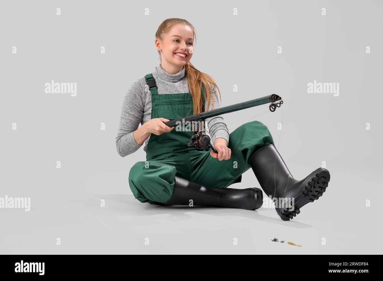 Sitting young woman with fishing rod on light background Stock Photo ...