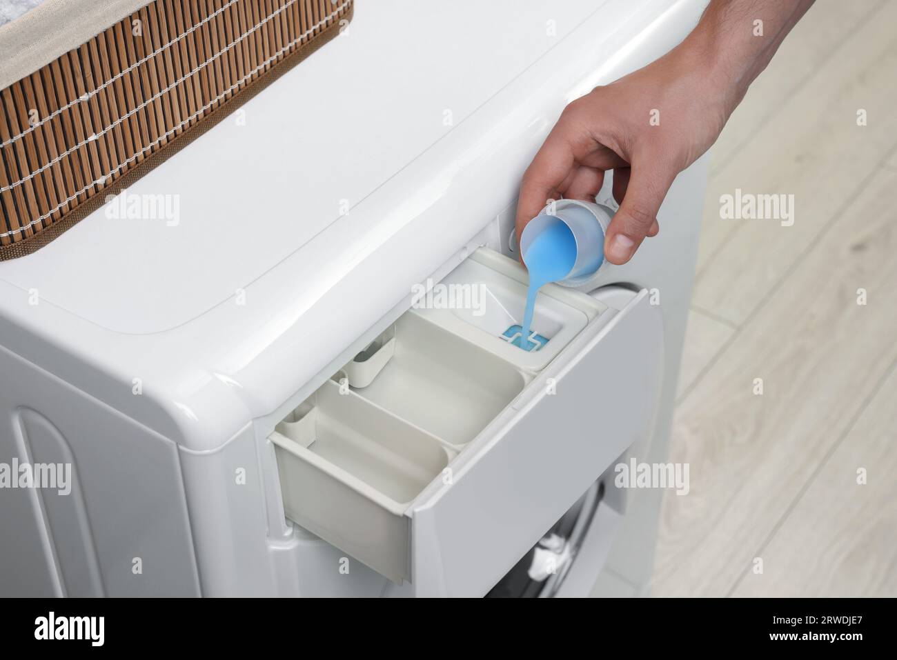 Man pouring fabric softener from cap into washing machine indoors ...