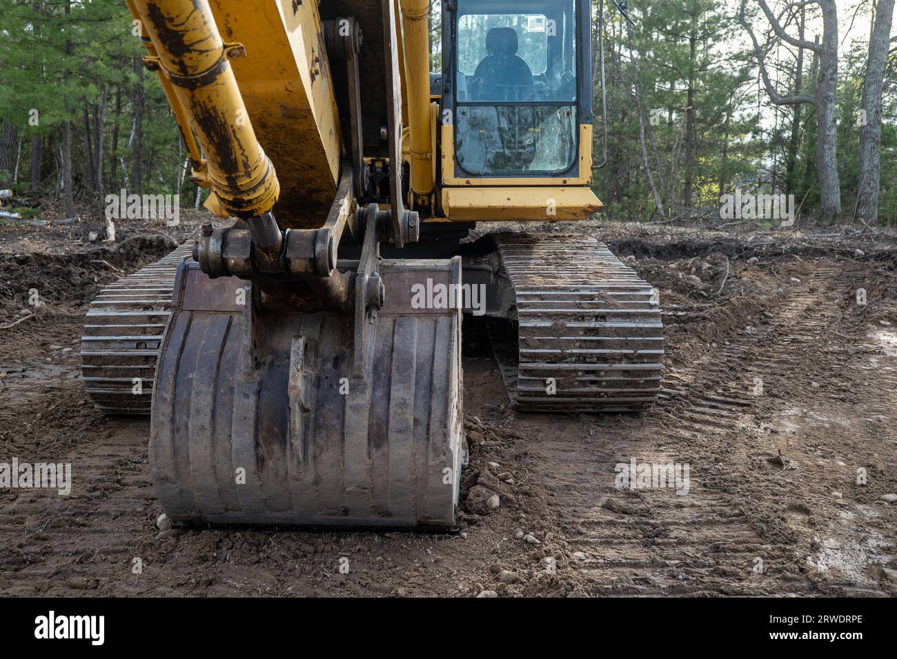 Closeup of the bucket and tracks of an excavator on the soil near trees ...