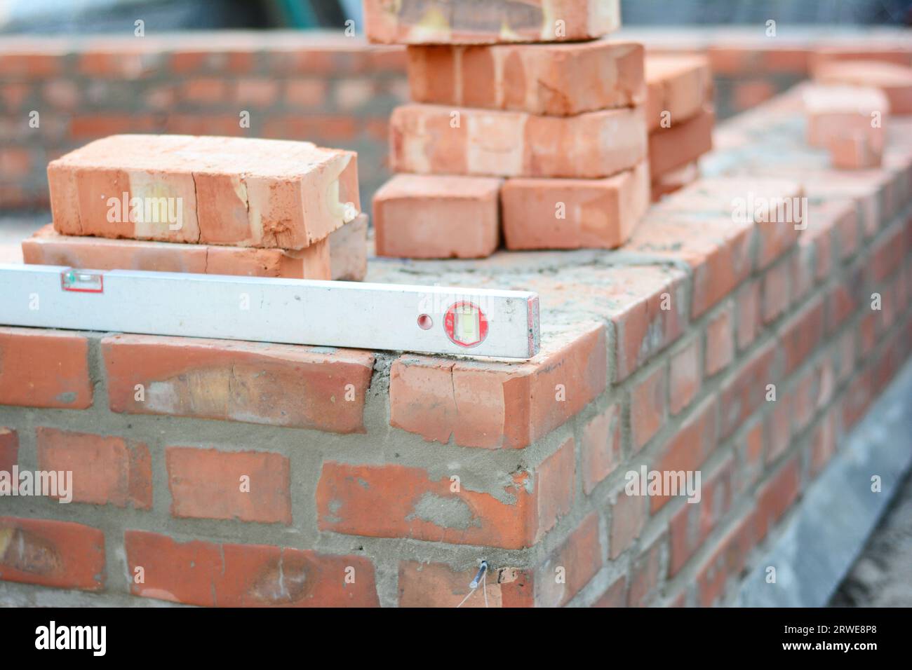 Building red brick house wall with spirit level and pile of bricks ...