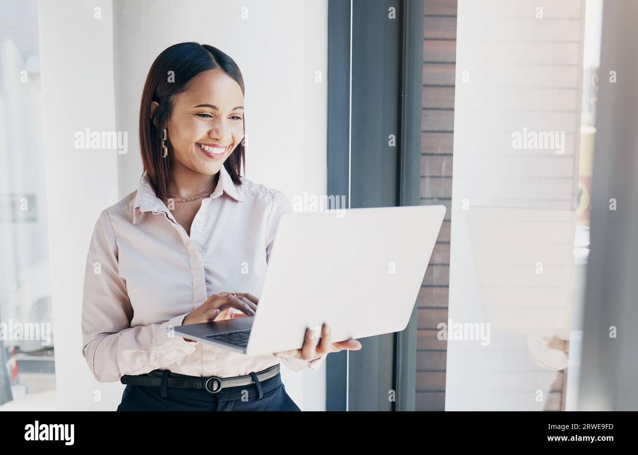 Happy woman at office window, with laptop and reading email research, schedule or online for ...