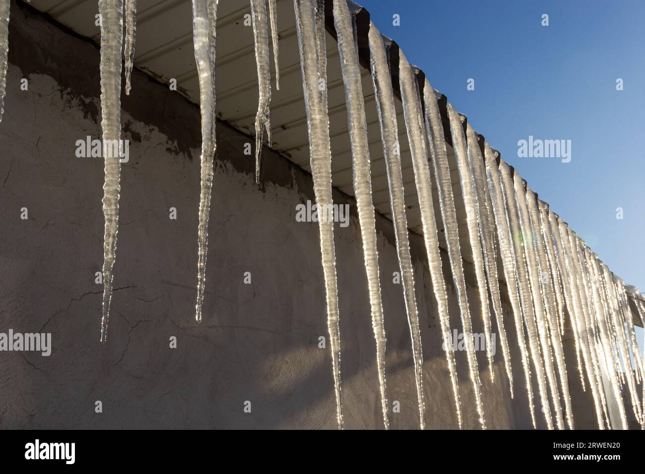 Sharp icicles and melted snow hanging from the eaves of the roof ...