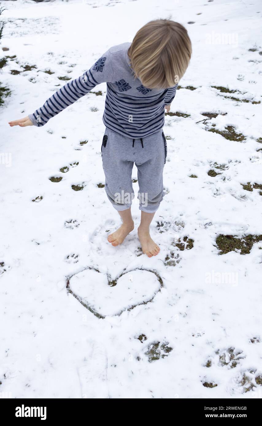 child walks barefoot on freshly fallen snow in winter. A heart is drawn ...