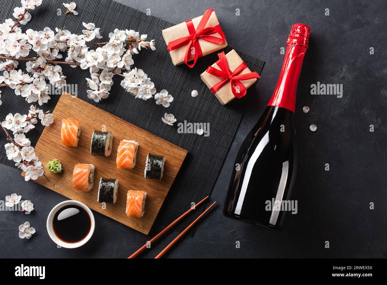 Set of sushi, maki rolls, gift boxes and bottle of champagne with branch of white flowers on ...