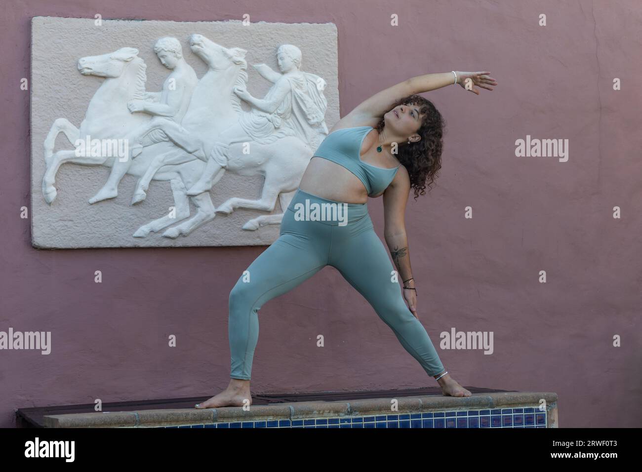 A young woman outdoors gracefully stretches with a vibrant mural as her ...
