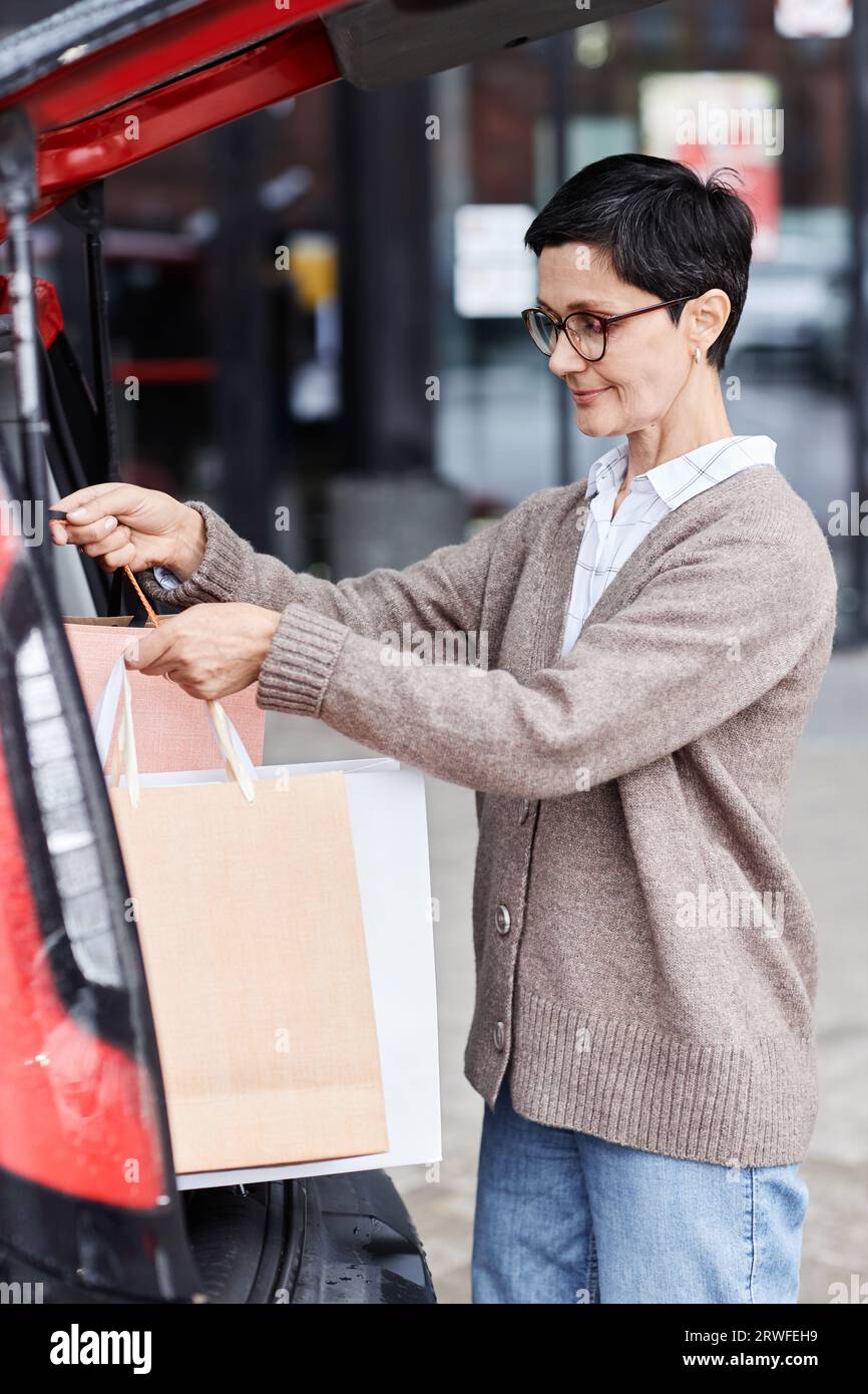 Side view portrait of adult woman putting shopping bags on car trunk ...