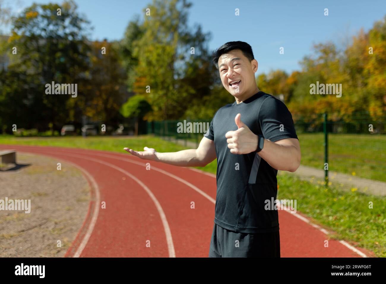 A young Asian male runner is standing in sportswear at the stadium and ...