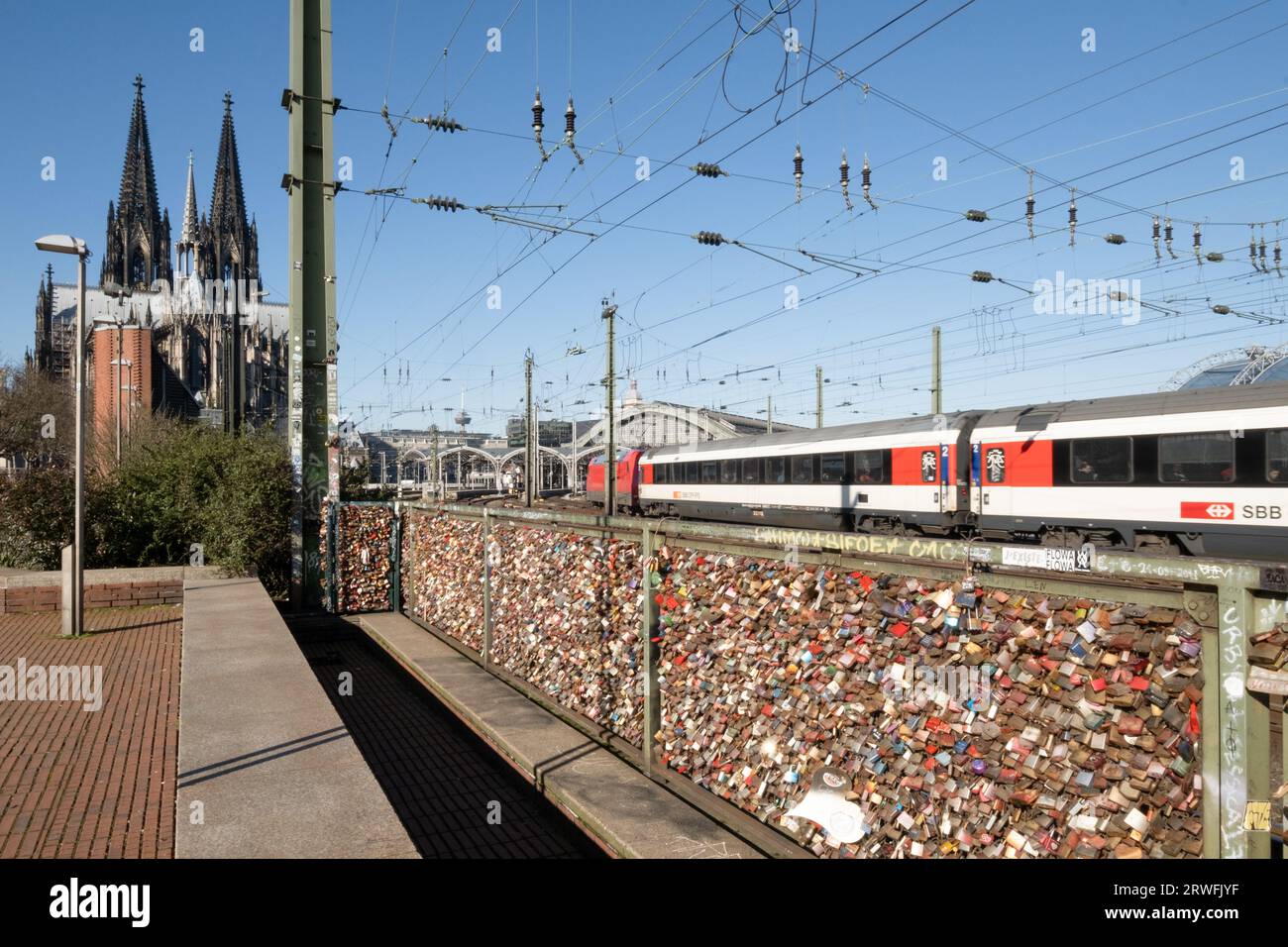Train leaving Cologne train station, with a fence covered in 'love lock ...