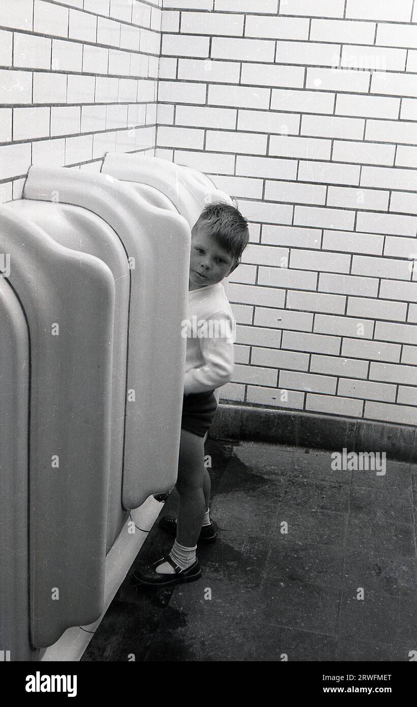 1960, historical, inside a tiled public lavatory, a little boy standing ...