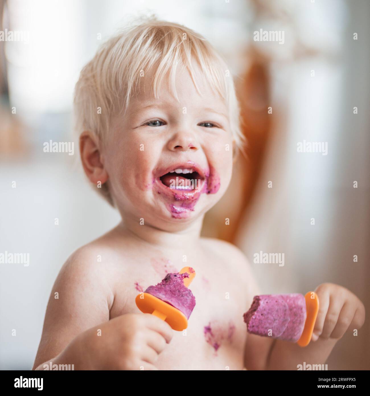 Happy adorable infant baby boy child smiling while eating two frozen ...