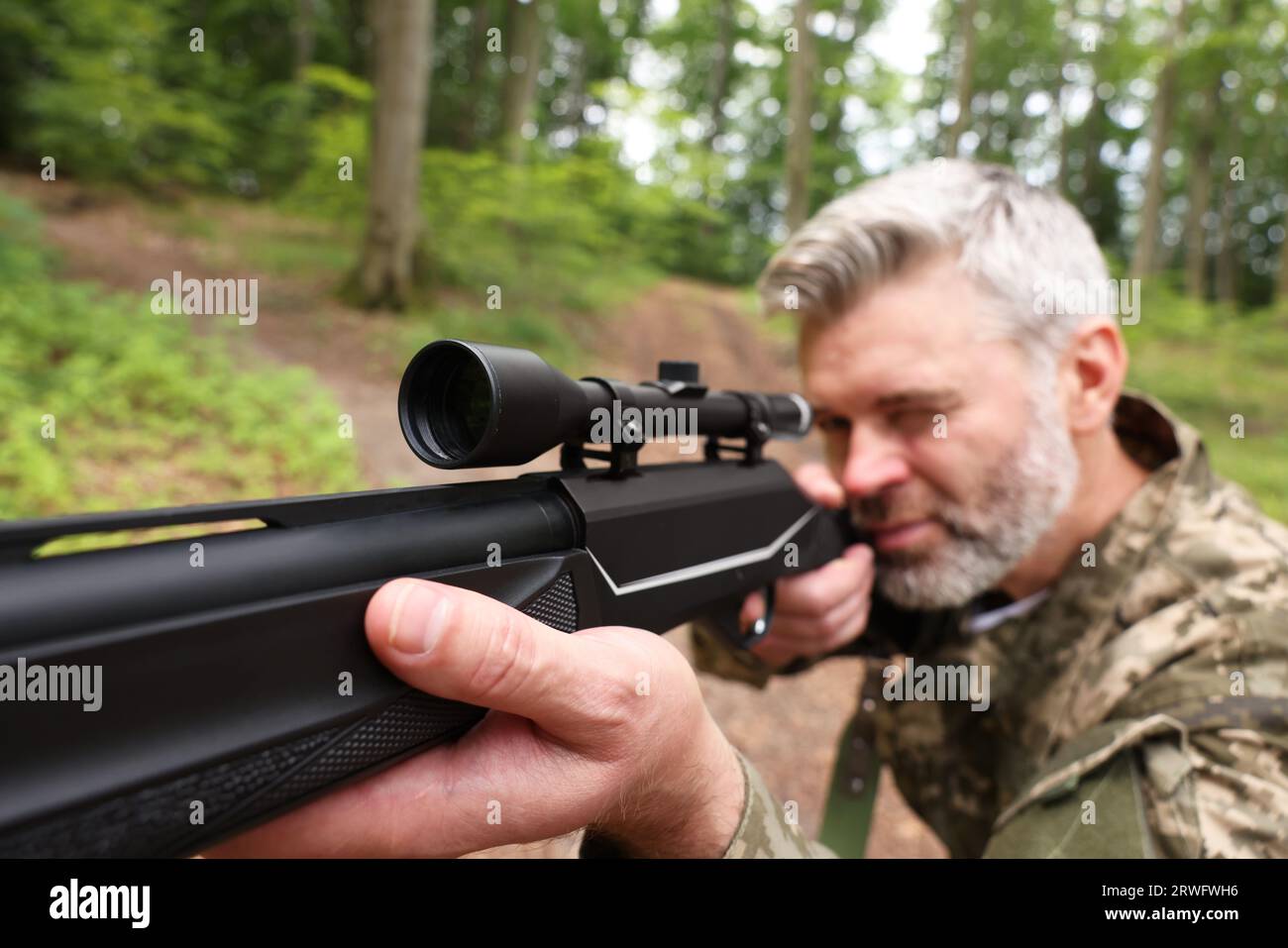 Man wearing camouflage and aiming with hunting rifle in forest ...