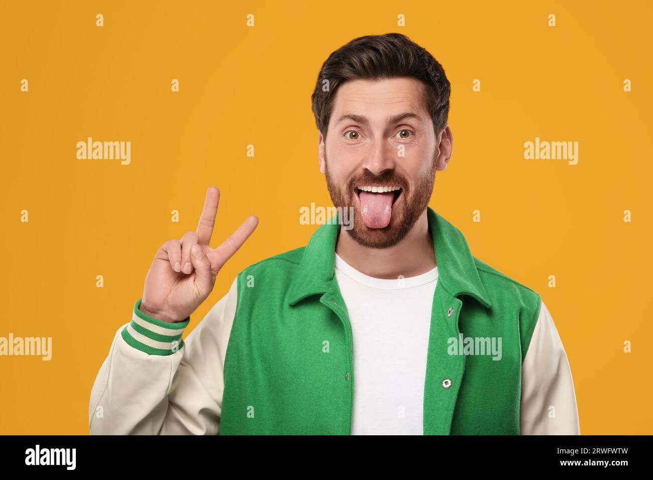 Man showing his tongue and V-sign on orange background Stock Photo - Alamy