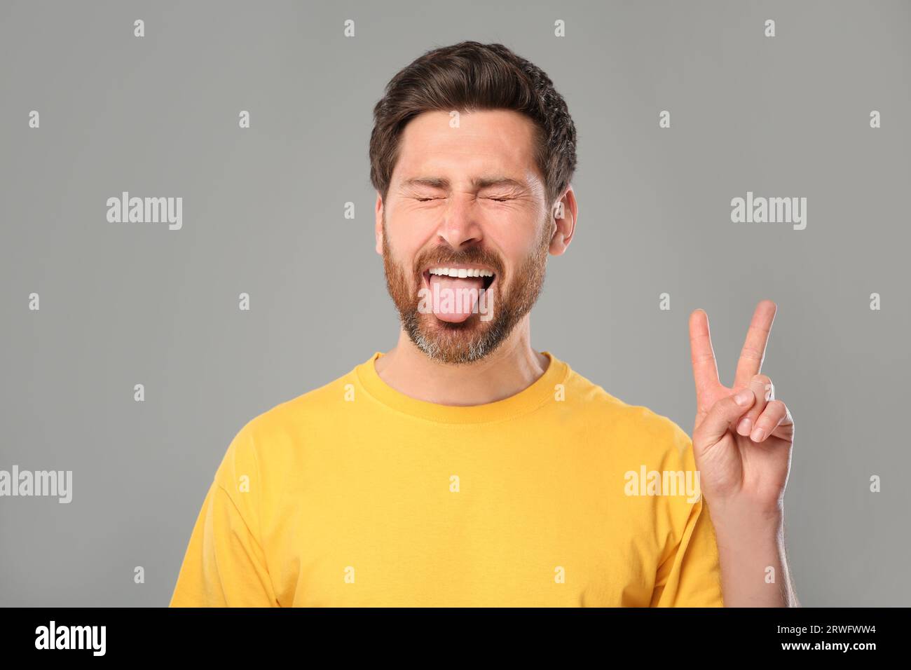 Man showing his tongue and V-sign on gray background Stock Photo - Alamy