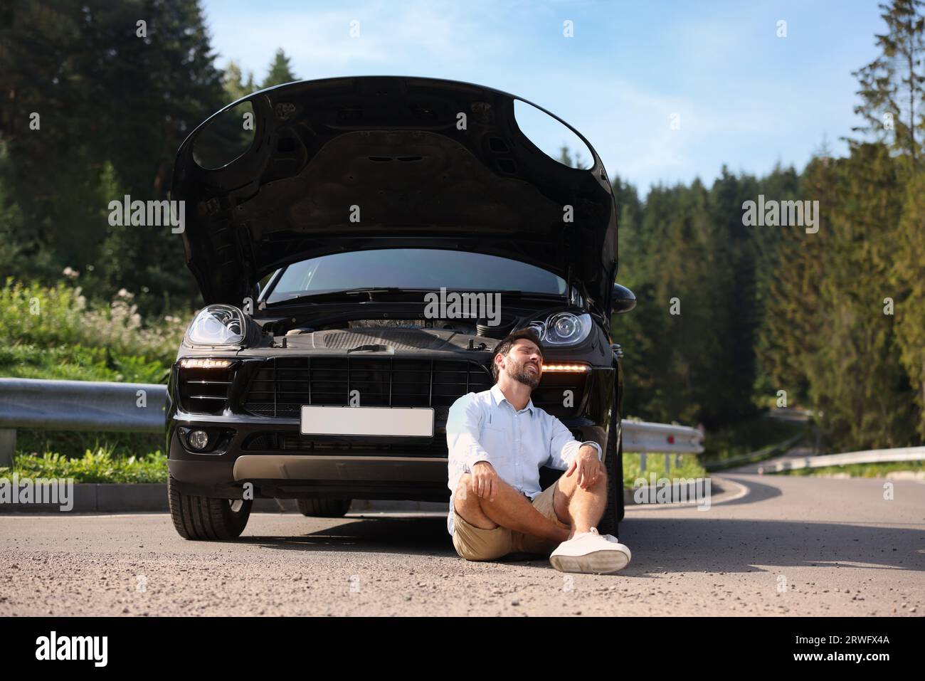 Stressed man sitting on asphalt road near broken car outdoors Stock ...