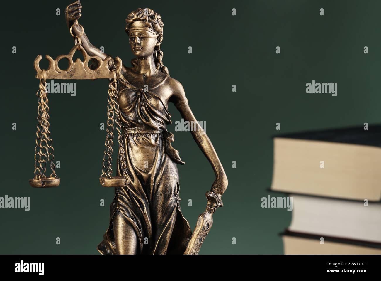 Statue of Lady Justice near books on green background, closeup and ...