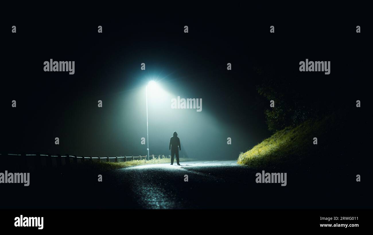 A spooky hooded figure standing under a street light on a atmospheric ...