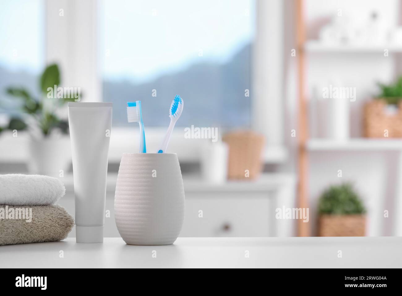 Plastic toothbrushes in holder, toothpaste and towels on white table ...