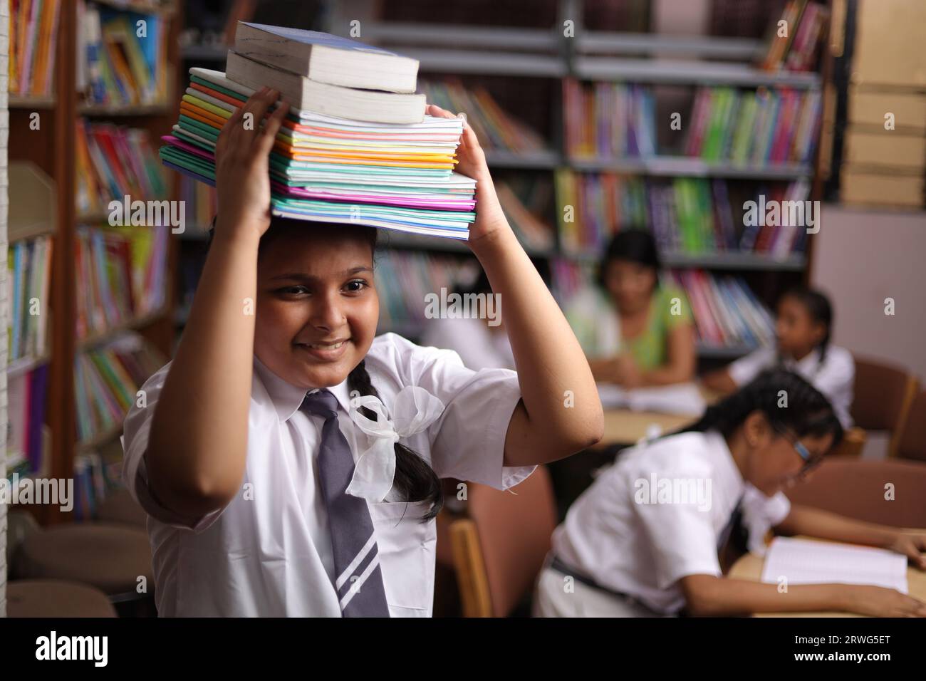 Happy teenager girl student holding books on her head, standing in library, hard work, exam ...