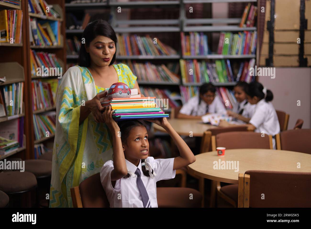 Indian teacher giving a bundle of heavy books on girl child teenager ...