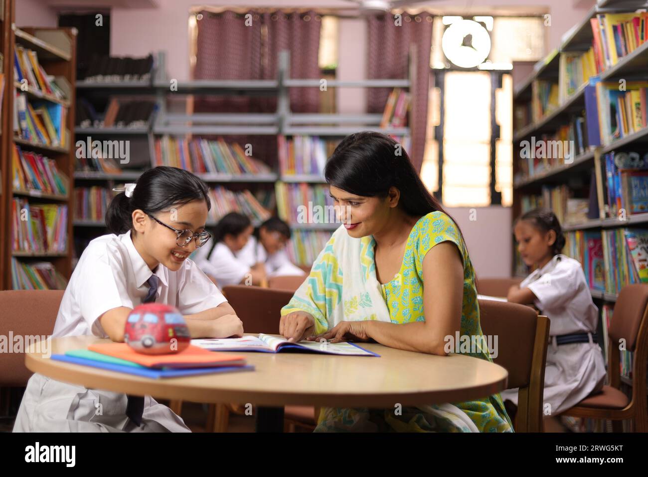 Confident school teacher teaching, educating girl child student in library, extra classes ...