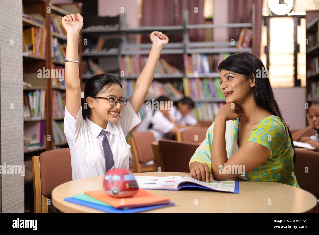 Confident school teacher teaching, educating girl child student in library, extra classes ...