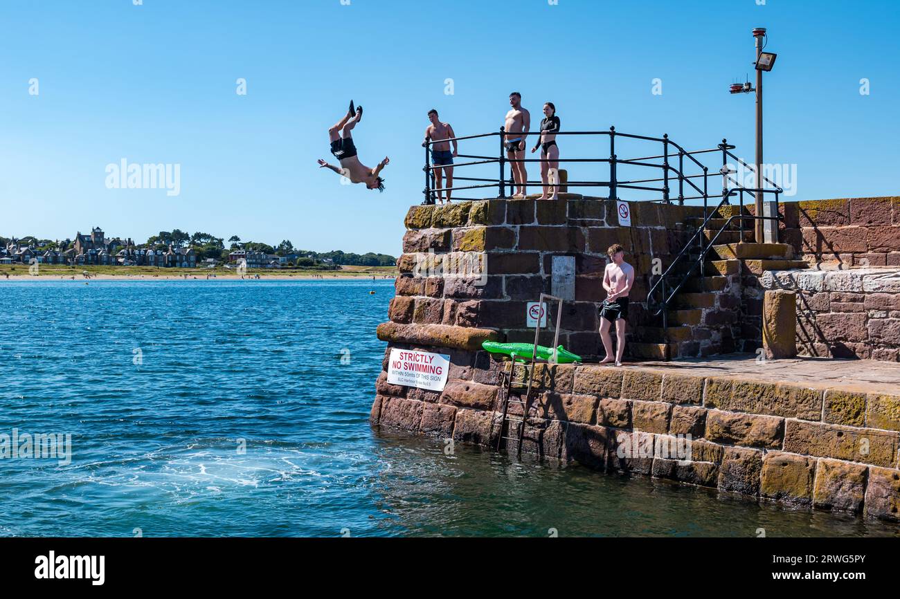 Boy somersaulting into sea from quayside in hot Summer weather, North ...