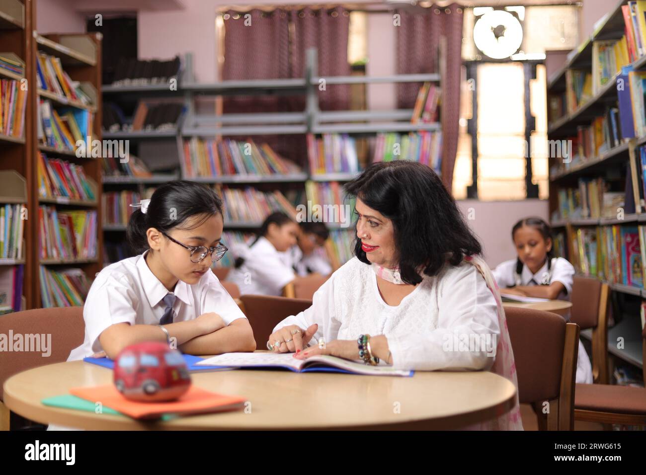 Confident school teacher teaching, educating girl child student in library, extra classes ...