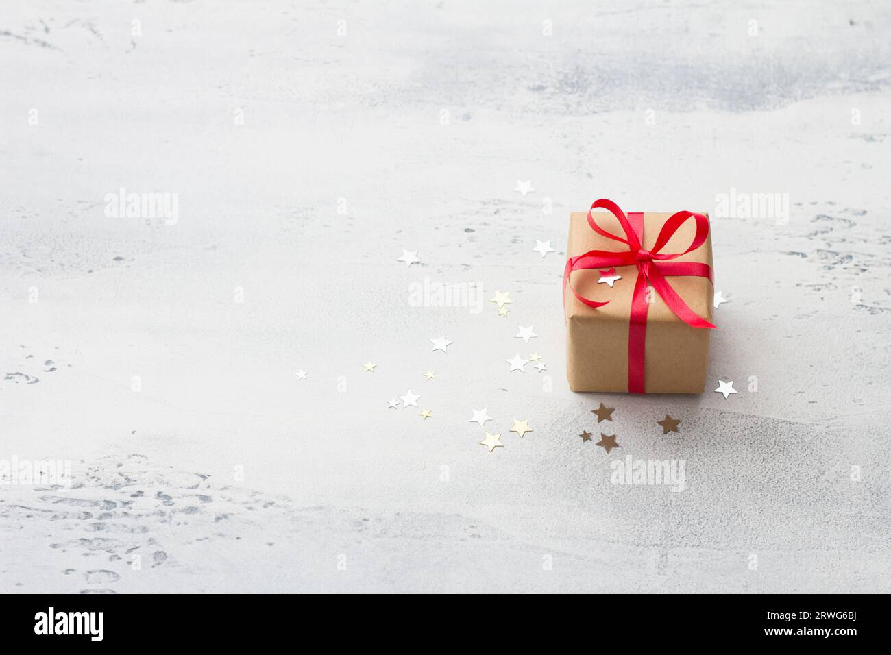 A small gift wrapped in kraft paper with a red ribbon on a light blue ...