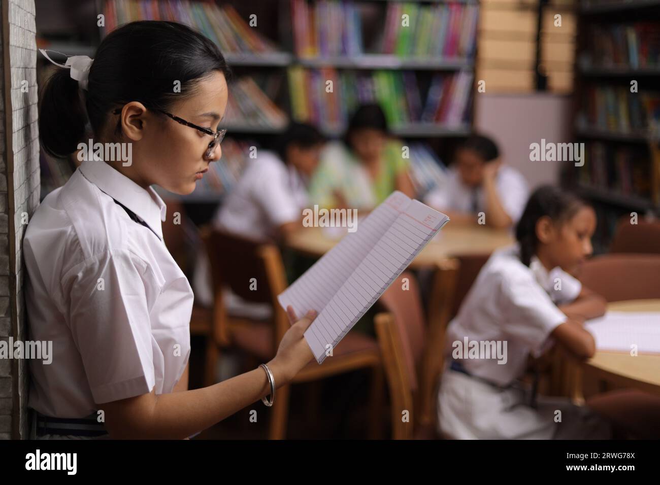 Smart student leaning against wall, reading a book in hand, focused ...