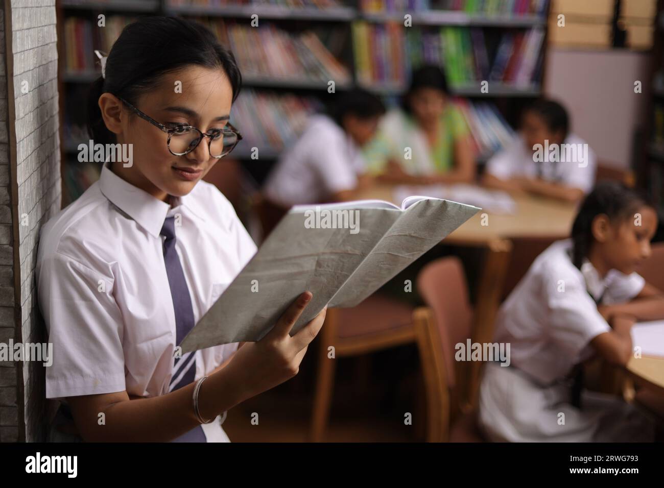 Smart student leaning against wall, reading a book in hand, focused ...