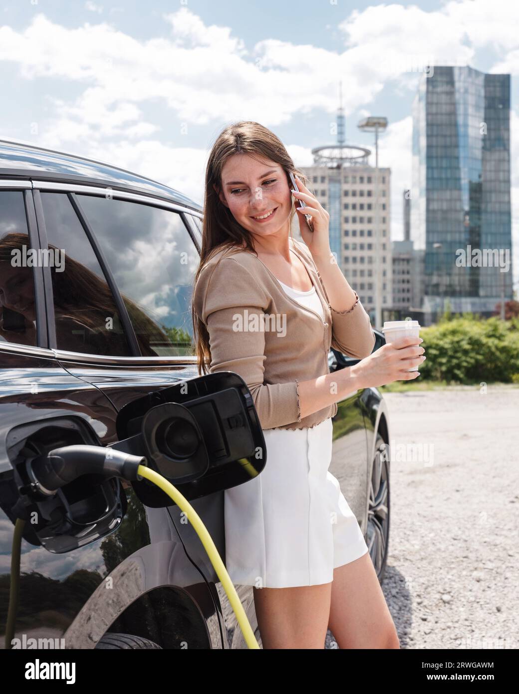 Beautiful girl plugging a cable charger into her parked black electric ...