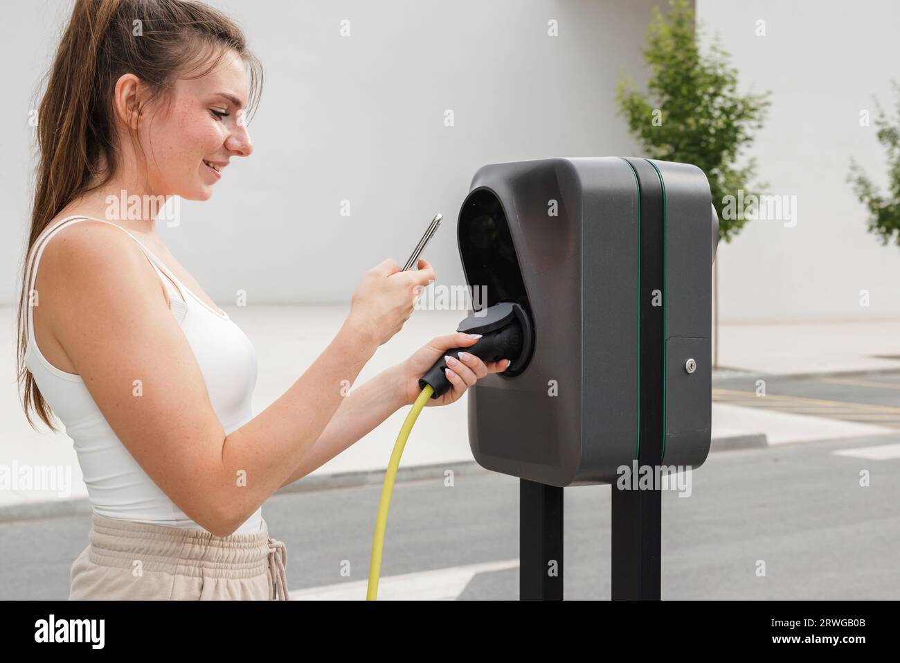 Girl connecting her electric car and a charging station with a cable charger and pressing a ...
