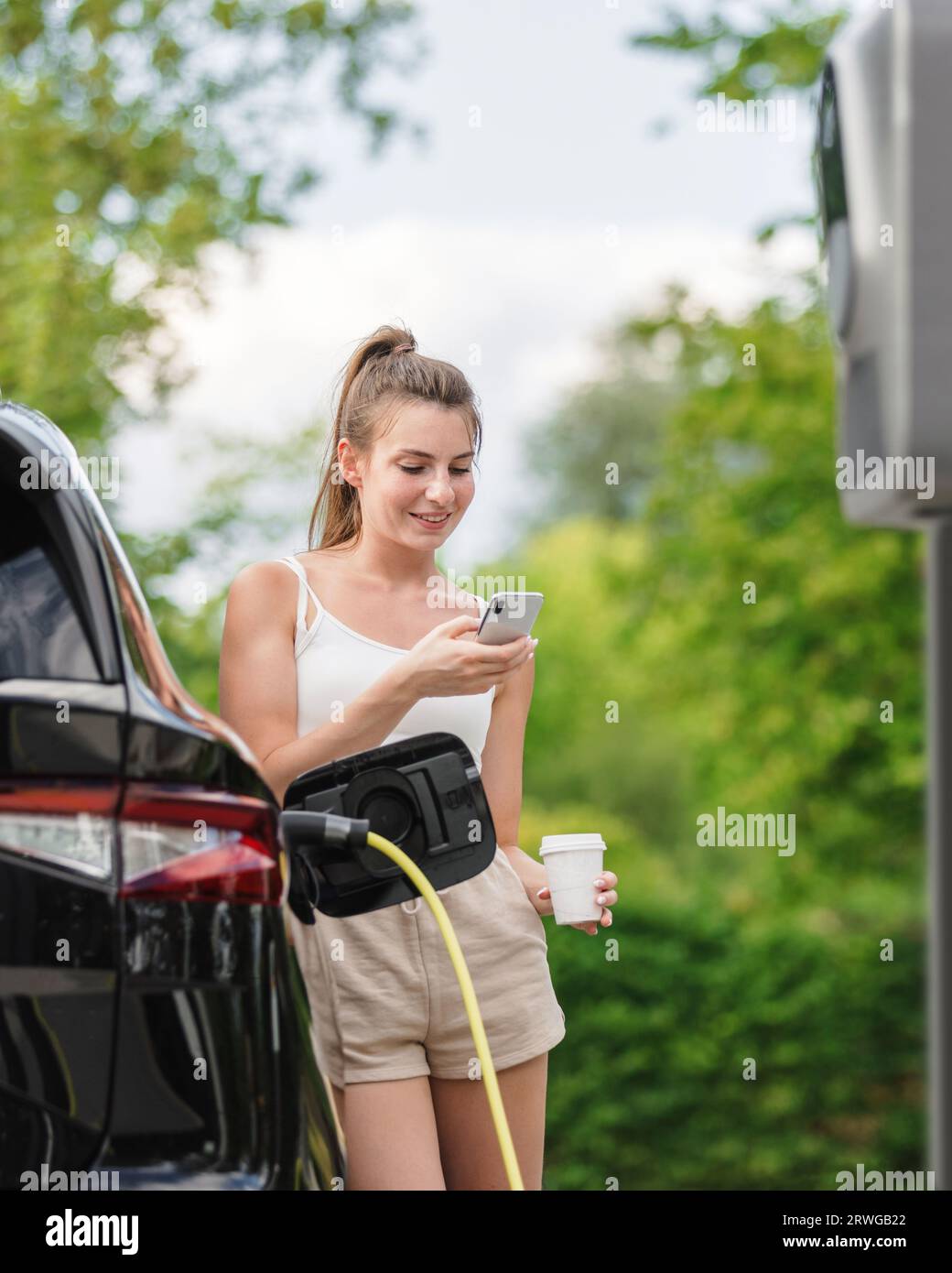 Beautiful girl plugging a cable charger into her parked black electric ...