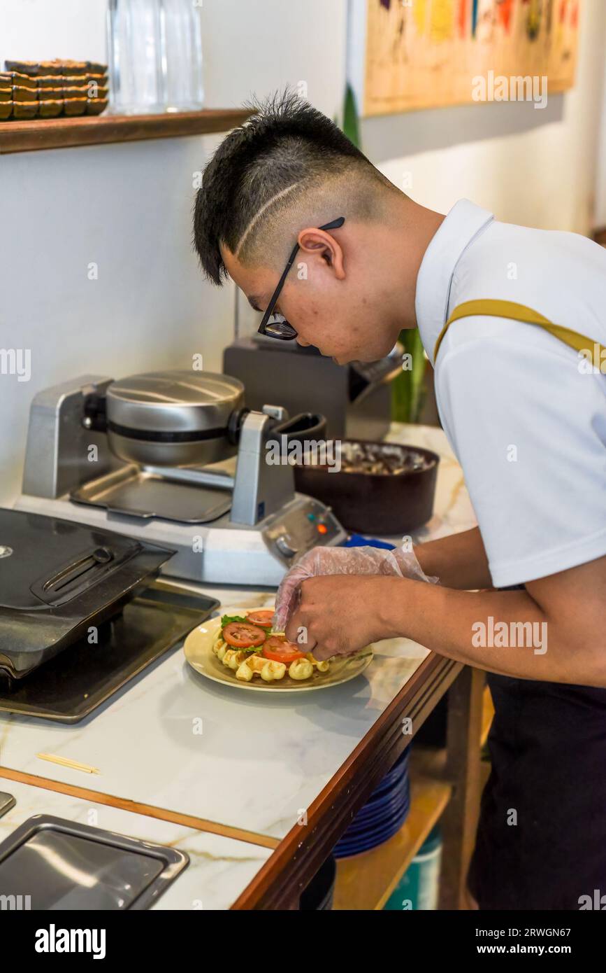 Vietnamese man chef serving fresh belgian waffles with chicken, cheese ...
