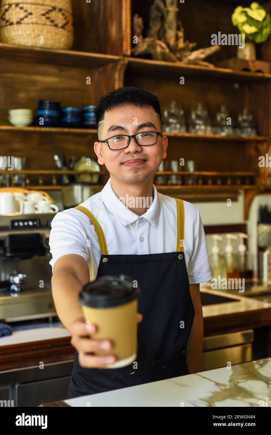 Vietnamese smiling waiter holding paper cups with coffee in a cafe ...
