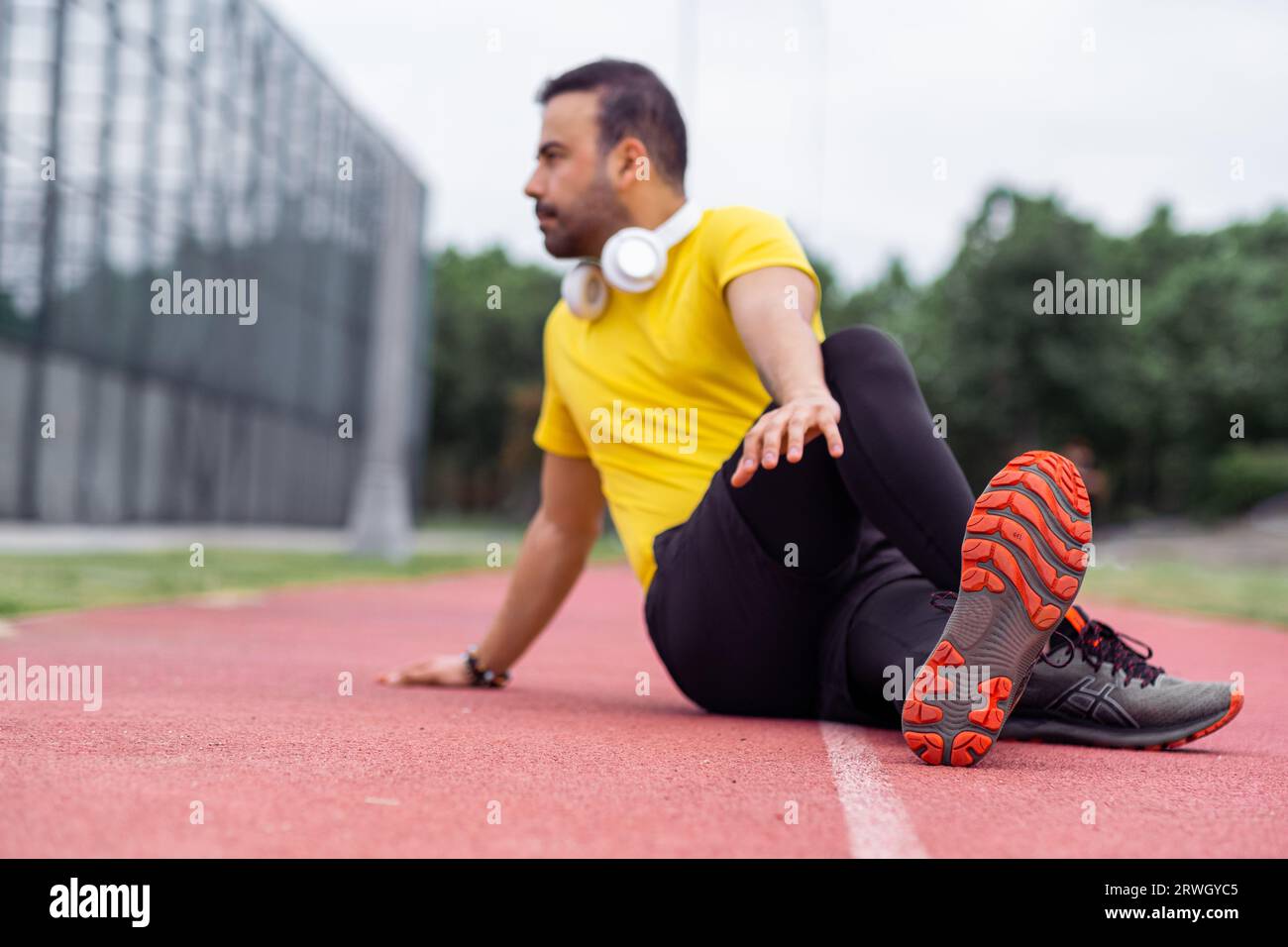 Man in activewear doing body twisting exercise sitting on track on ...