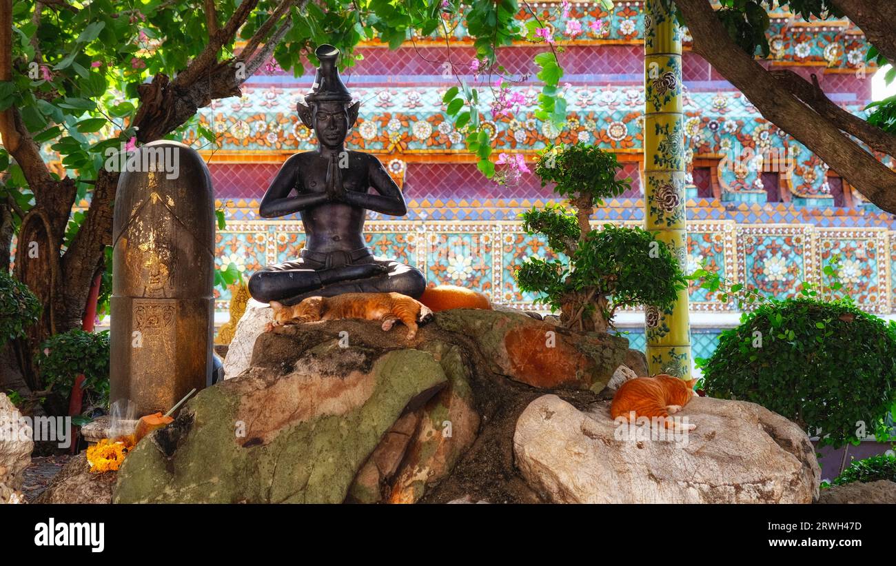 A meditating figure statue in a garden with orange cats and trees Stock ...