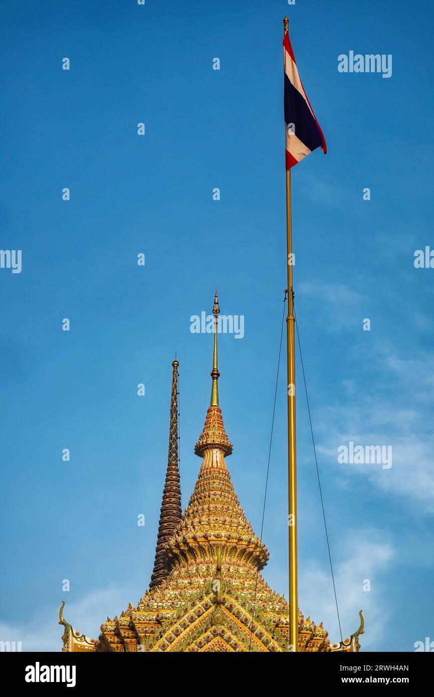 A Thai temple spire and flag against a blue sky. The temple spire is ...