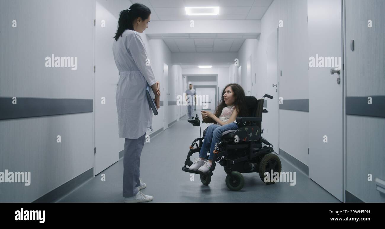 Hospital corridor: Woman with SMA disability in wheelchair talks to ...