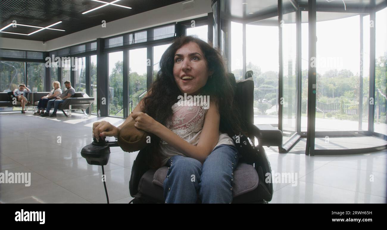Woman with SMA disability rides in clinic entrance on motorized ...