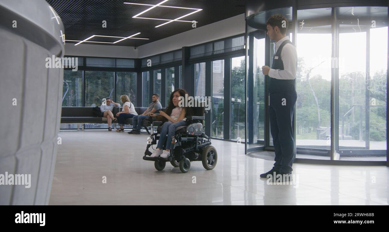 Woman with SMA disability rides in clinic entrance on motorized ...