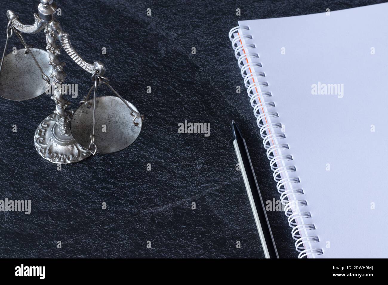Ancient balance scales, blank notebook, and pen on dark background ...