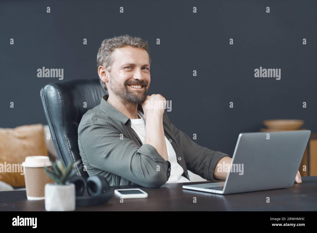 Smiling man finds joy in work as he diligently operates laptop on well ...