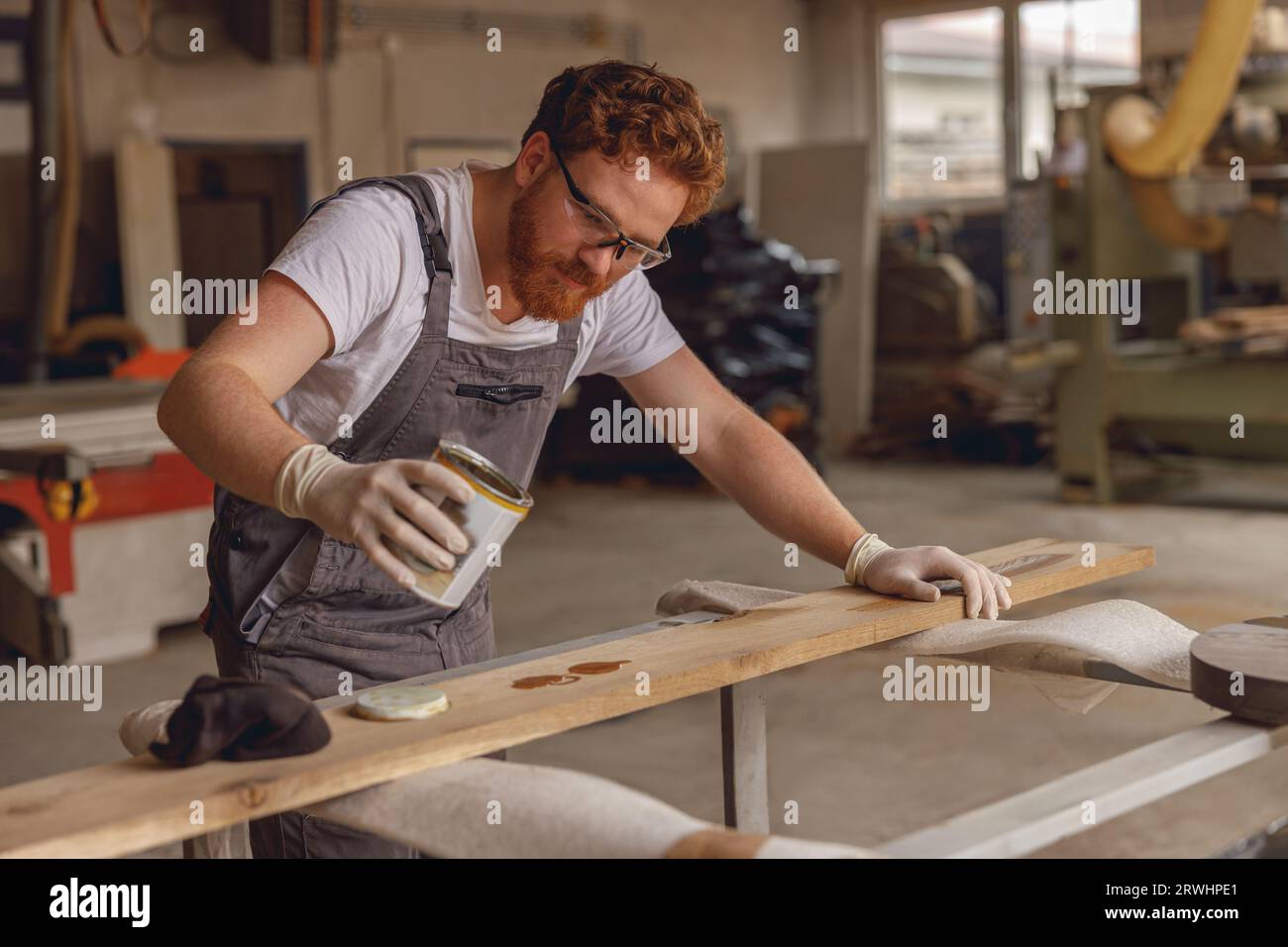 Craftsman coating a wooden board with protective oil in a workshop ...