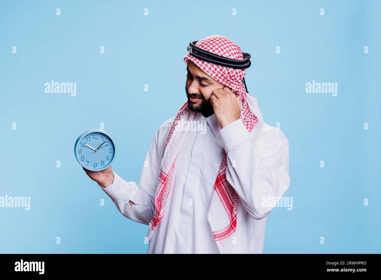 Man wearing traditional muslim clothes holding retro alarm clock and ...