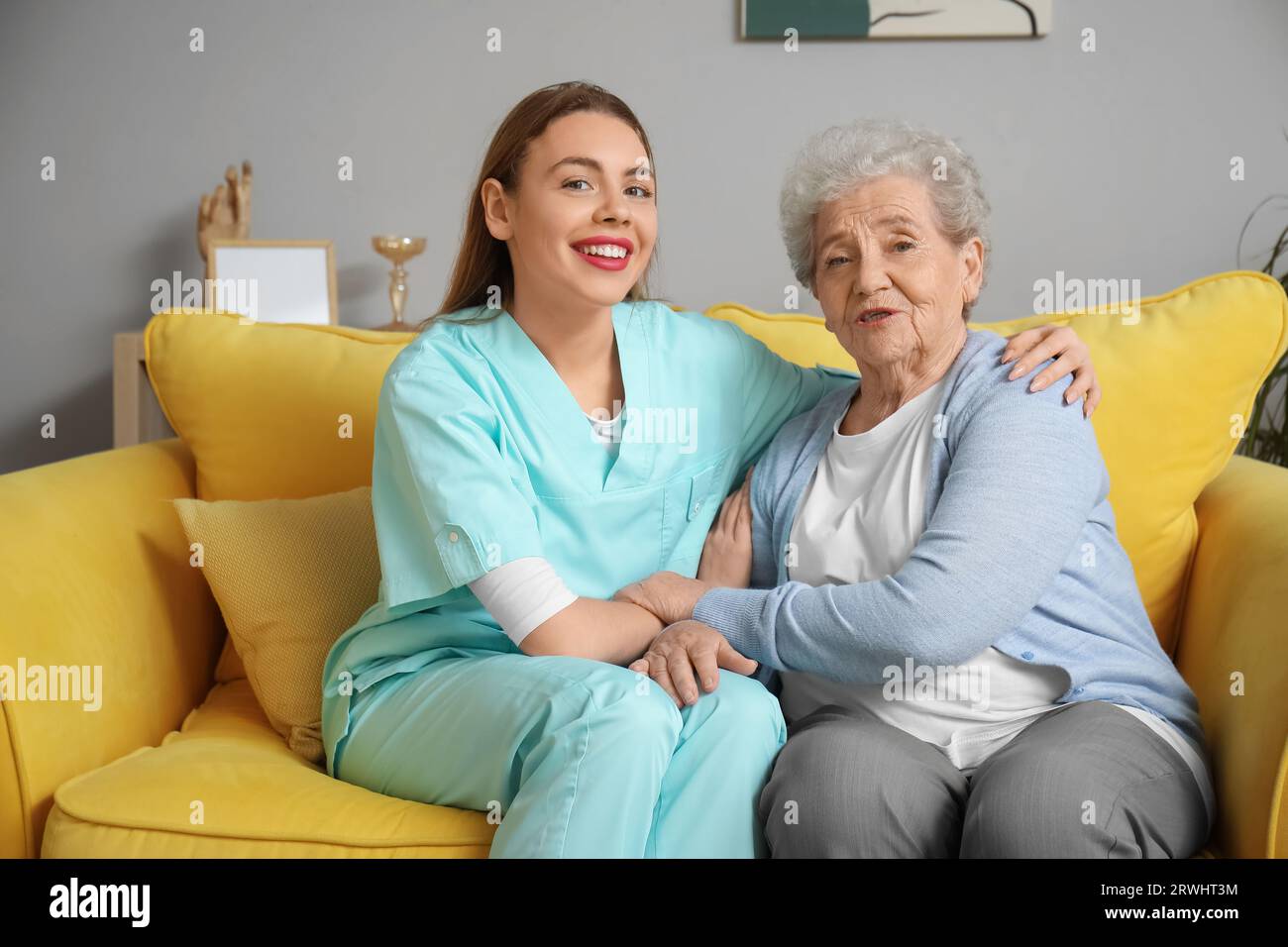 Female caregiver with senior woman sitting on sofa at home Stock Photo ...