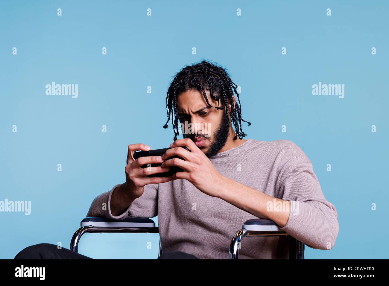 Focused gamer with disability playing on smartphone with tensed facial ...
