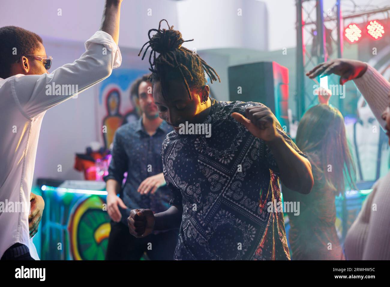 Young cheerful man dancing with friends in dark nightclub with vibrant ...