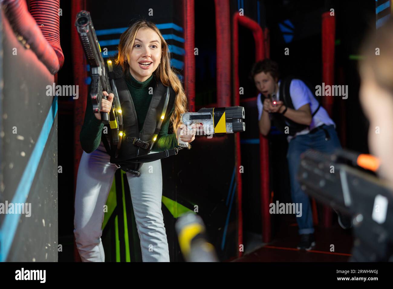 Joyous girl with laser pistol playing laser tag with friends on ...
