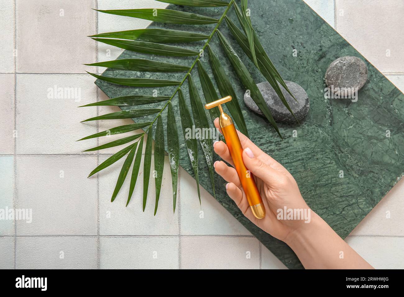 Female hand with metal face massage roller on light tile background ...